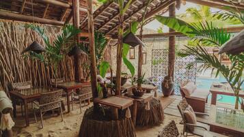 Uma área externa com mobiliário rústico, piscina e plantas tropicais.