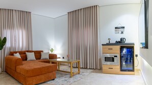 Uma sala de estar moderna com sofá, mesa de centro e uma pequena cozinha equipada com micro-ondas e cafeteira.