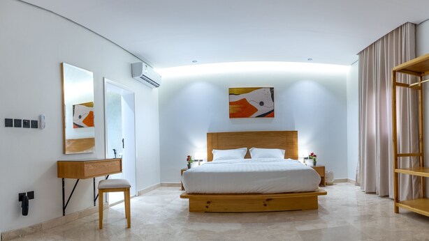 Quarto moderno com cama de madeira, mesa de cabeceira, espelho, ar condicionado fixado na parede e prateleira de madeira.