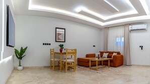 Uma sala de estar moderna com televisão de tela plana, área de jantar com mesa e cadeiras, sofá e planta em vaso.