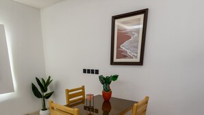 Uma sala de jantar com uma mesa de vidro, cadeiras de madeira, um vaso com planta e um quadro na parede.