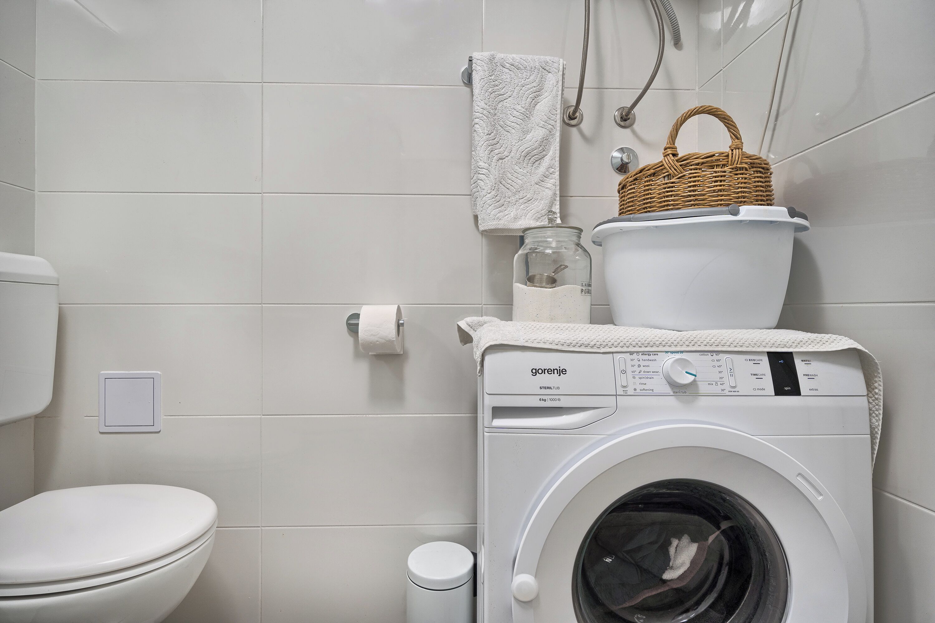 Casa de banho moderna com sanita branca, máquina de lavar roupa e chuveiro.