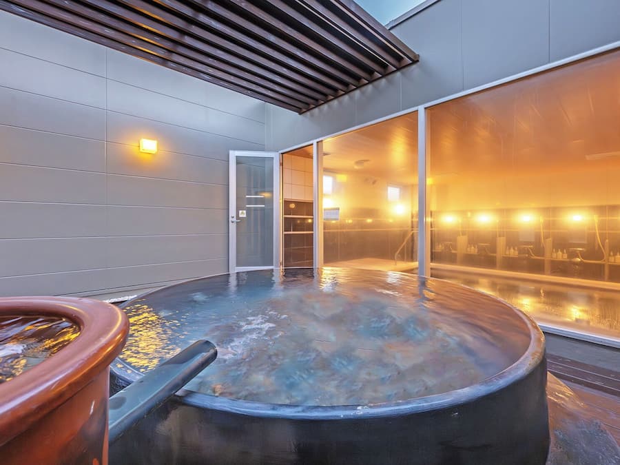 Uma área de spa moderna, com hidromassagem, uma grande fonte de água e uma sala de sauna com paredes de vidro.