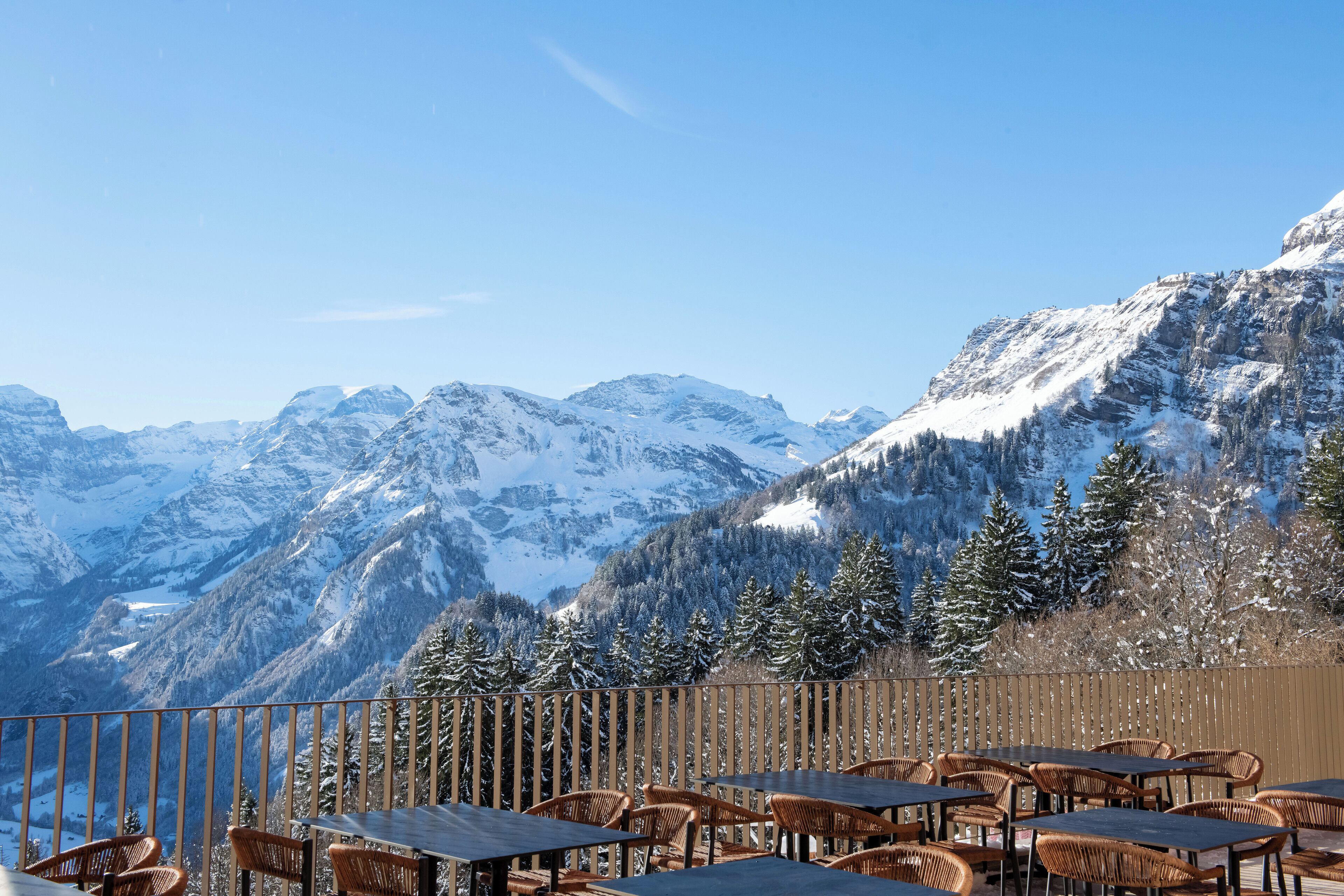 Terraço com mesas e cadeiras, com vista para montanhas cobertas de neve.