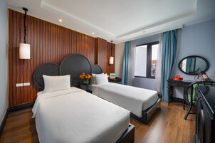 Quarto de hotel com duas camas, parede de painel de madeira, escrivaninha com espelho e janela com cortinas.