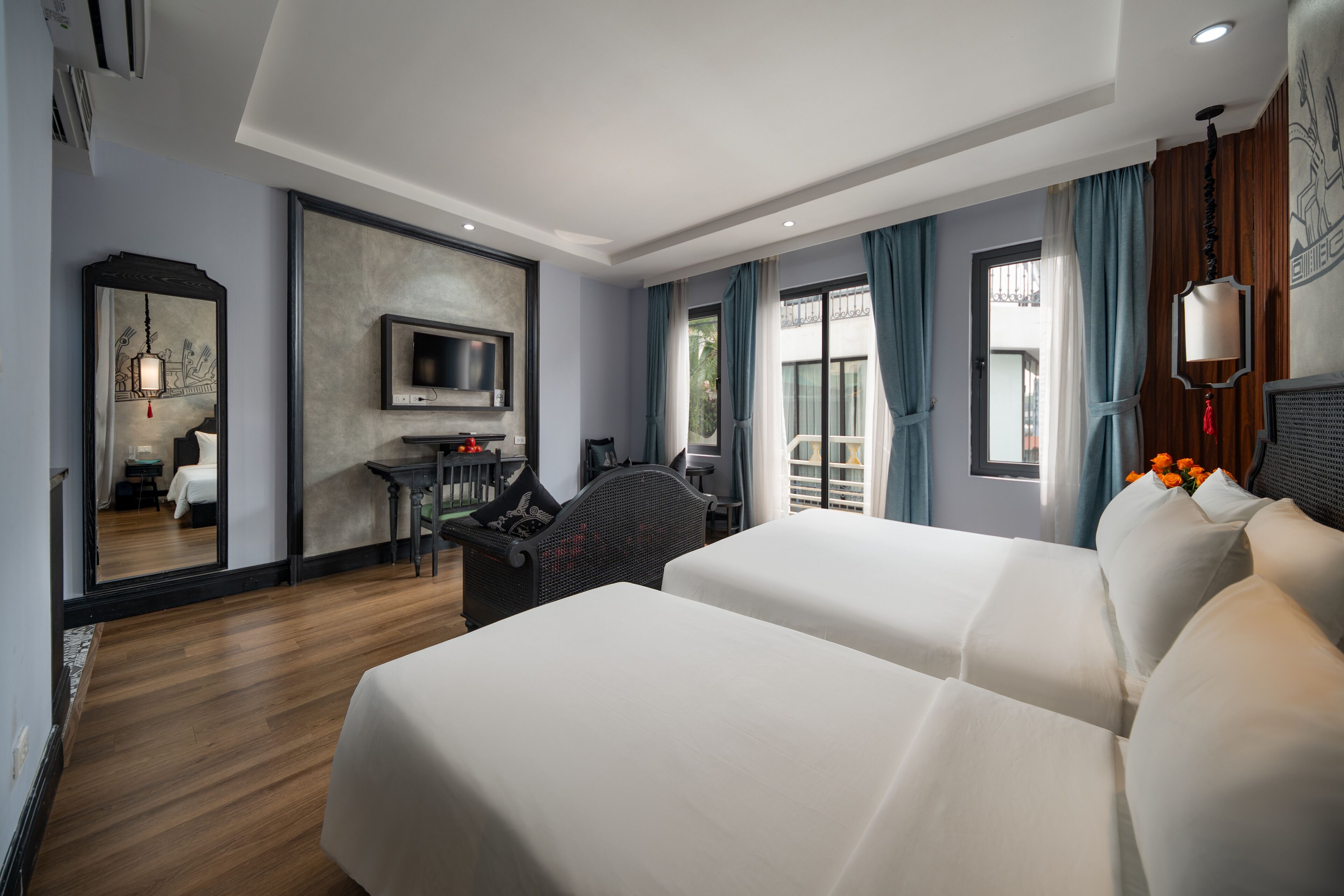 Quarto de hotel com duas camas, uma escrivaninha, uma cadeira, uma televisão e um espelho grande.