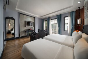 Quarto de hotel com duas camas, uma escrivaninha, uma cadeira, uma televisão e um espelho grande.