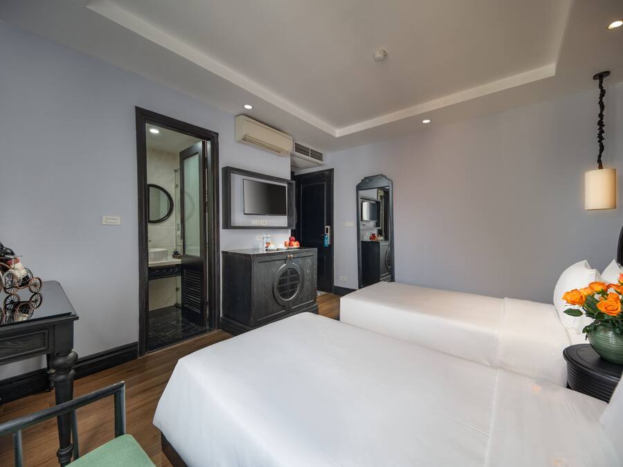 Quarto de hotel com duas camas, televisão, espelho, cômoda e uma pequena mesa com um vaso de flores.