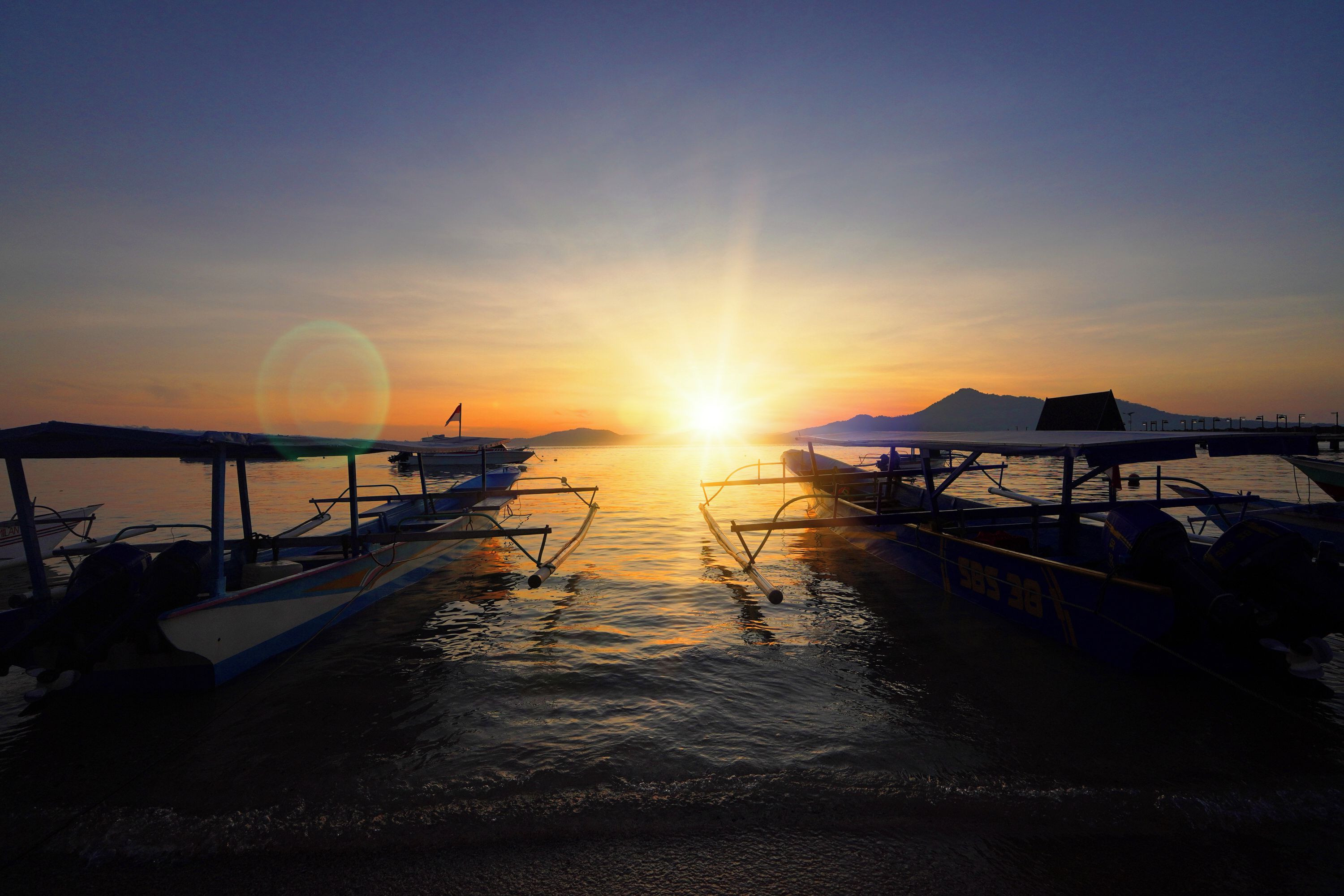 Pôr do sol sobre a água, com barcos atracados.