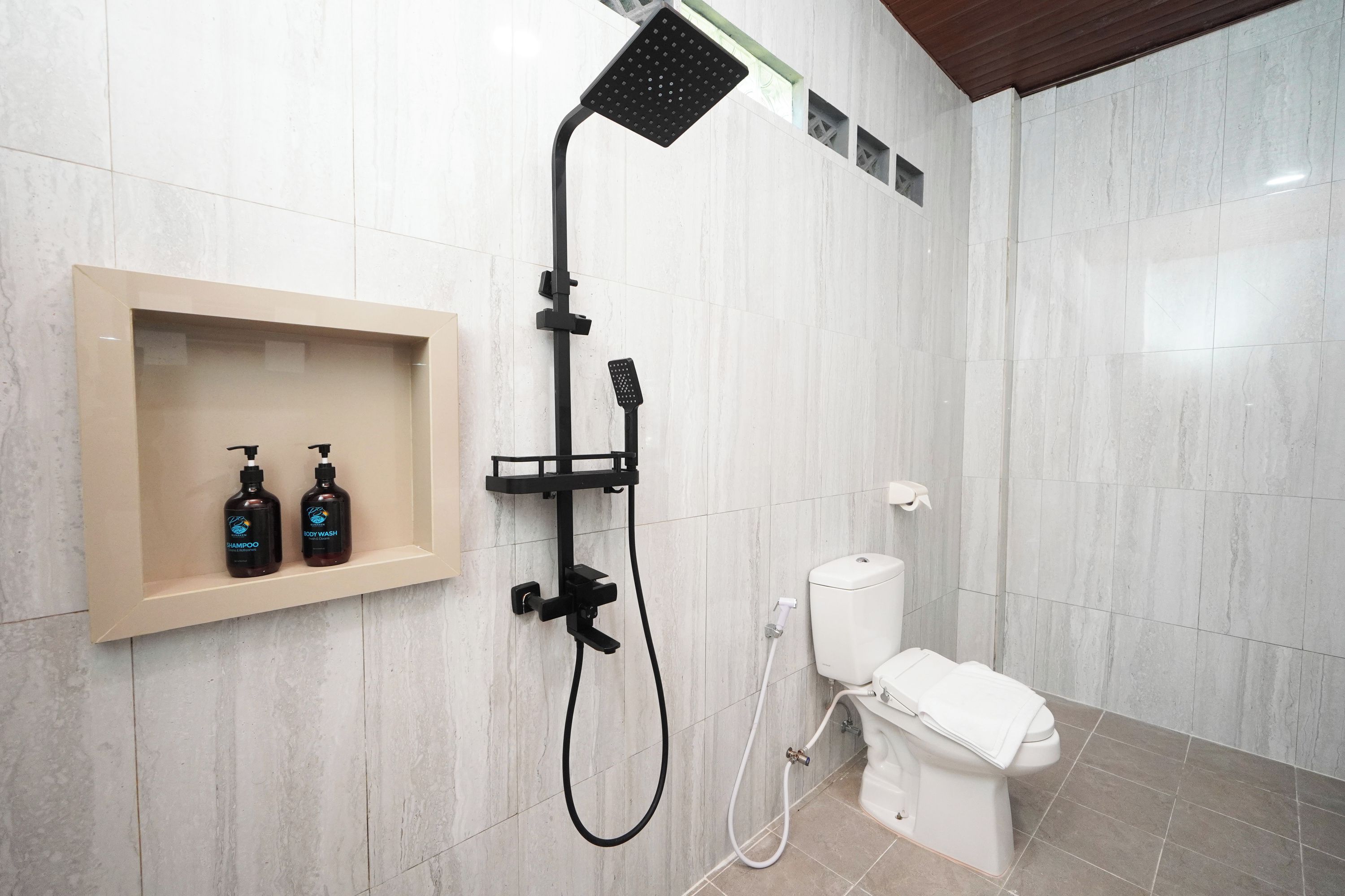 Casa de banho moderna com chuveiro, sanita e prateleira com dois frascos de champô e gel de banho.