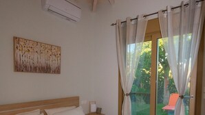Quarto com uma cama grande, ventilador de teto, aparelho de ar condicionado e vista para o exterior através de uma porta de vidro.