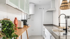 Cozinha moderna com armários brancos, bancada de madeira e piso estampado.