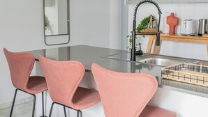 Uma cozinha moderna com uma ilha central, cadeiras cor-de-rosa e luminárias pendentes de vime.