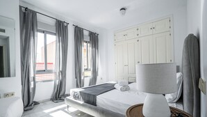 Quarto moderno com cama, luminária de cabeceira e vista para um prédio.