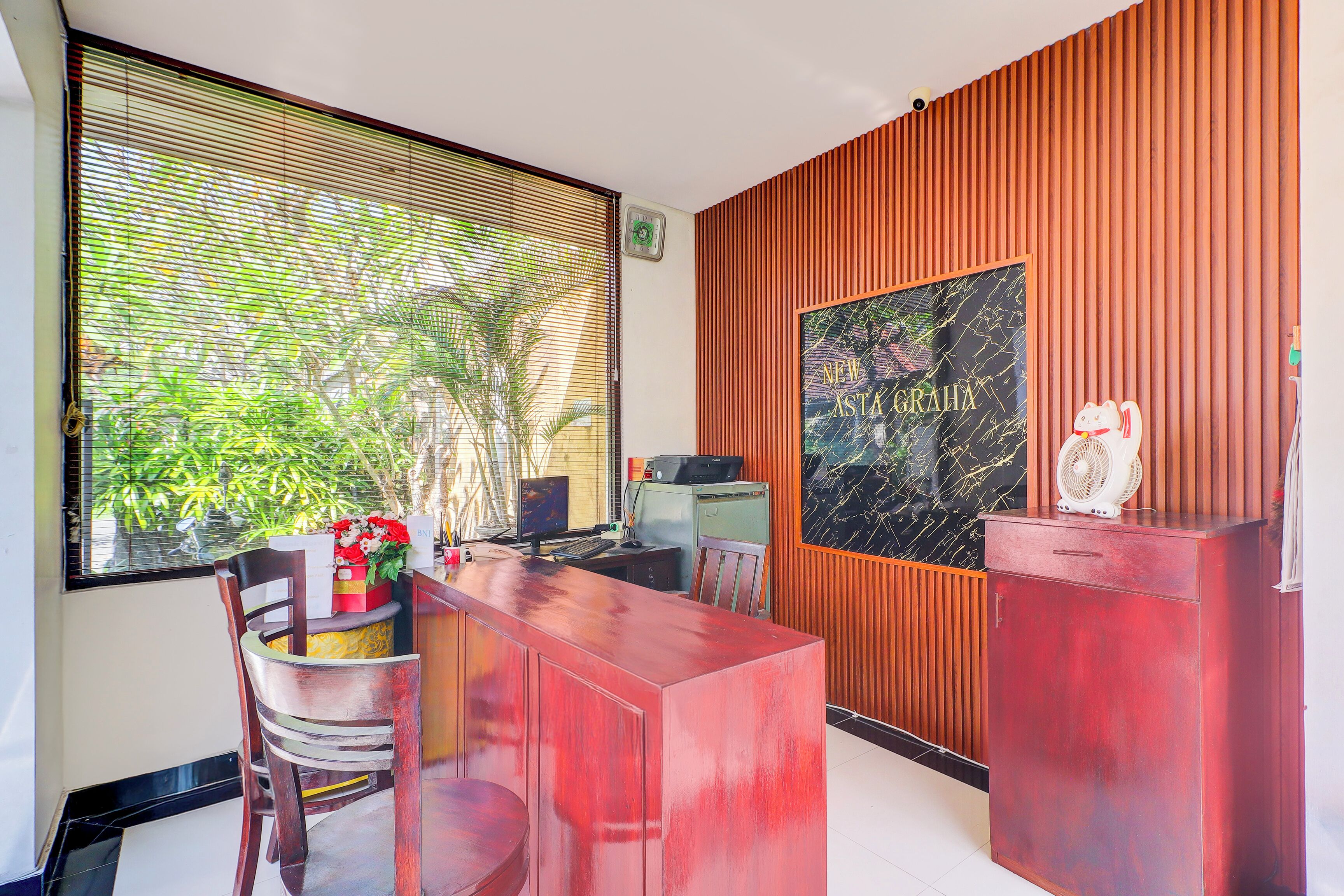 Quarto moderno com parede revestida de madeira, uma janela grande com persianas, uma escrivaninha com computador e um objeto decorativo em um armário.