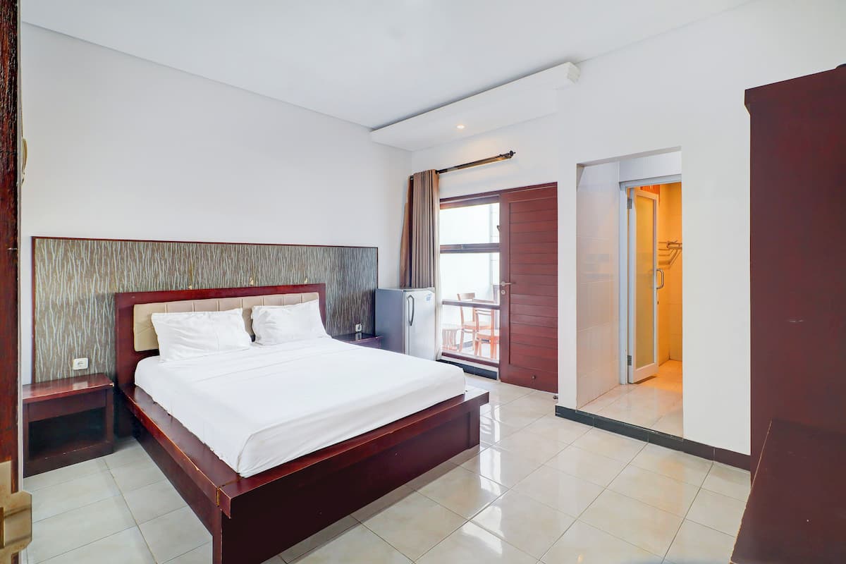 Quarto de hotel com cama de madeira, mesa de cabeceira, pequeno frigorífico e vista para a varanda.