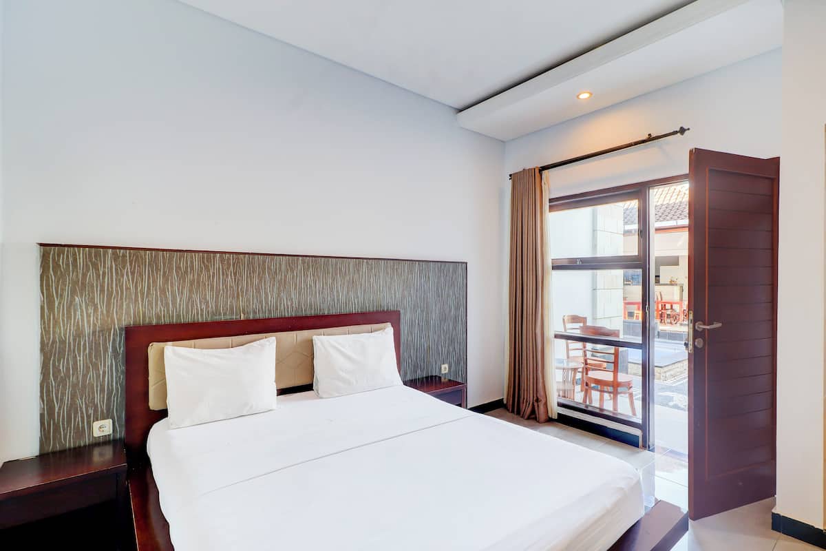Quarto de hotel com uma cama grande, cabeceira de madeira e vista para a área externa através da porta de vidro.