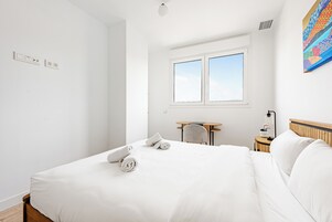 Quarto de hotel com uma cama grande, uma escrivaninha, uma cadeira e uma janela.