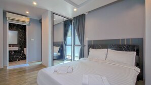 Quarto de hotel moderno com uma cama grande, banheiro com toucador de mármore e porta de vidro que dá para uma varanda.