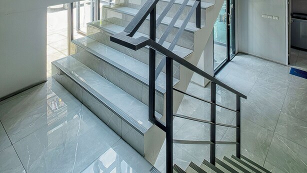 Um interior moderno com uma escada que leva a um segundo andar, janelas amplas e piso revestido de azulejos.