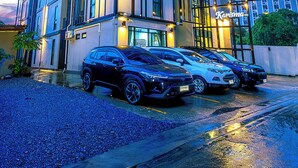 Um hotel moderno com fachada de vidro, vários andares e estacionamento com diversos carros.