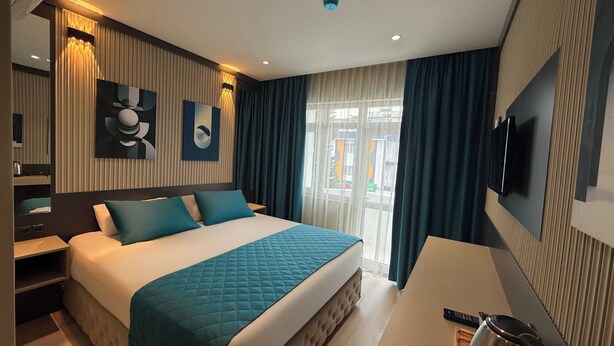 Quarto de hotel moderno com uma cama grande, uma escrivaninha, uma televisão e vista para o exterior.