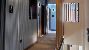 Corredor moderno de hotel com divisória de madeira, teto com iluminação embutida e piso carpeteado.