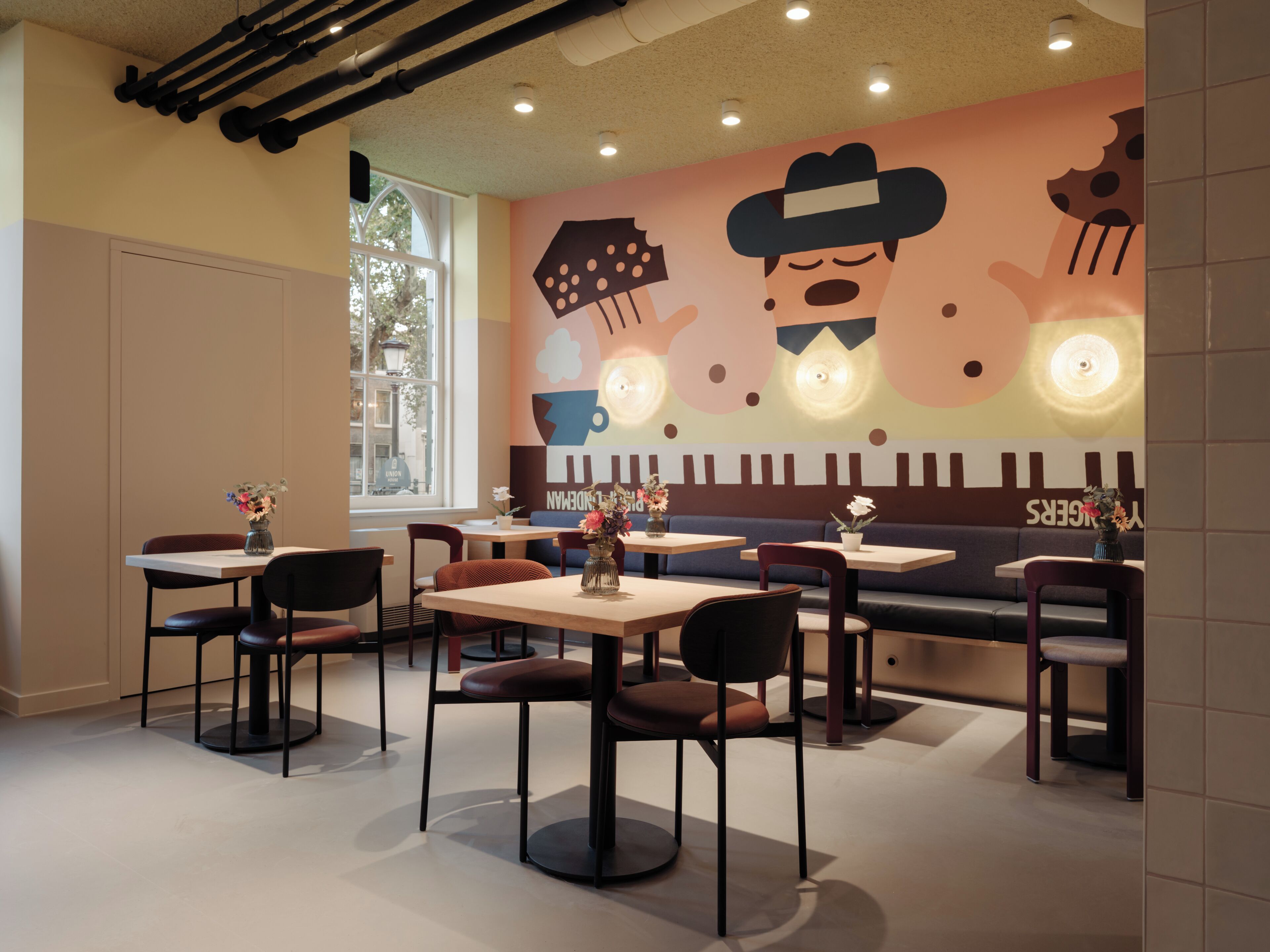 Um restaurante com cabines e mesas, um grande mural na parede e uma janela com vista para a rua.