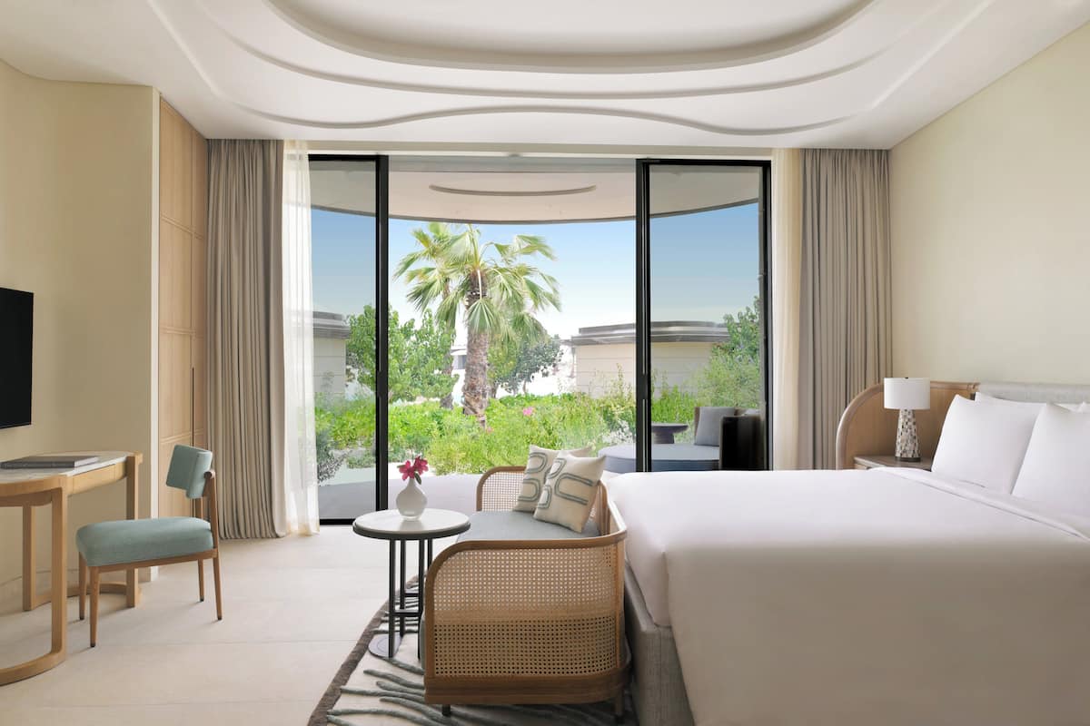 Quarto de hotel com uma cama grande, uma mesa pequena com uma cadeira, um sofá e uma televisão.