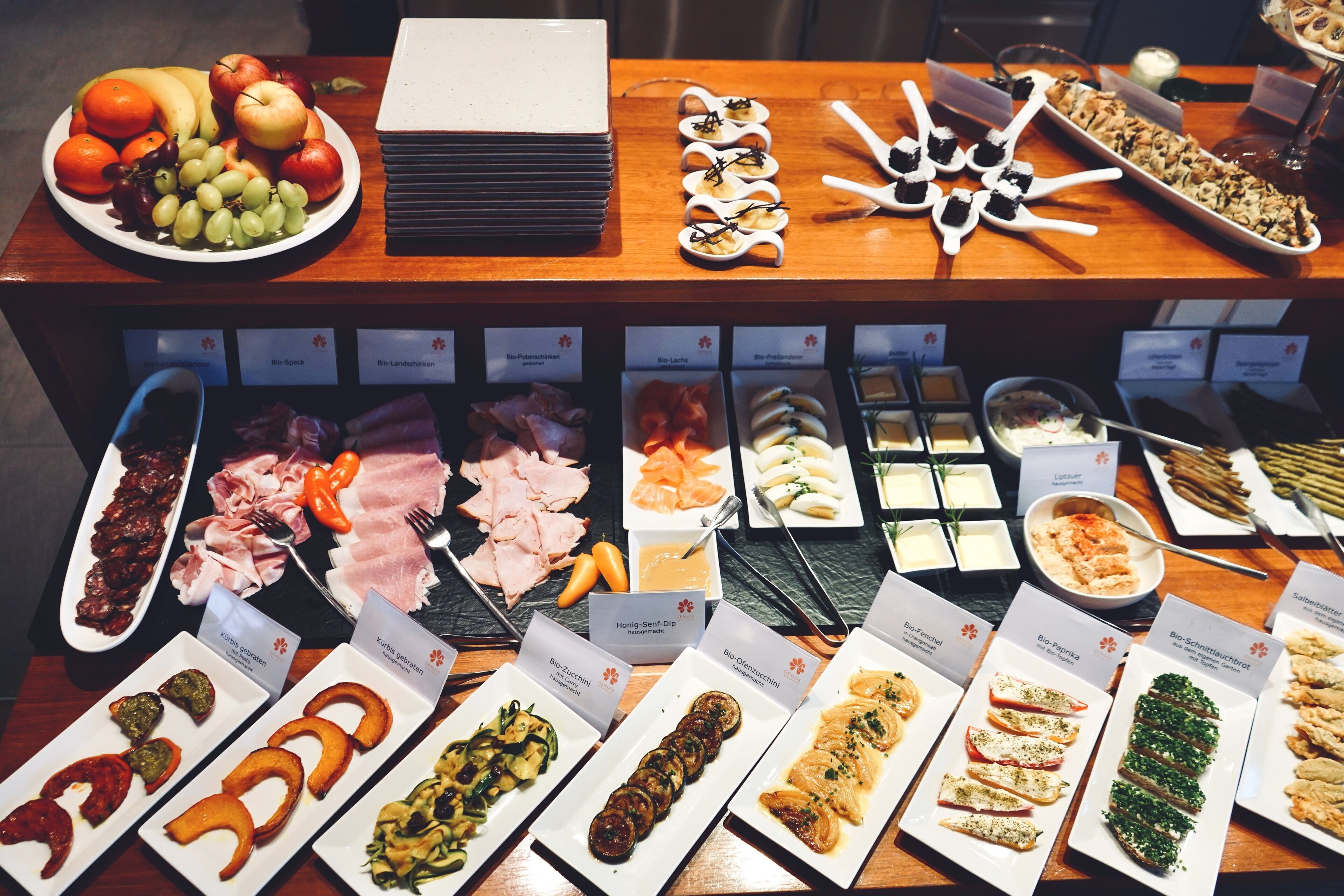 Buffet com diversas opções de comida, incluindo frutas, queijos, carnes e legumes.