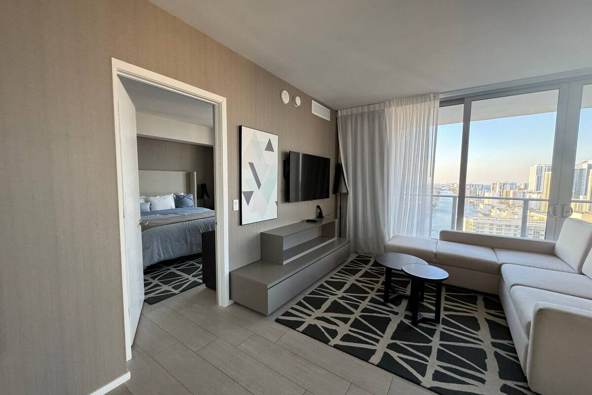 Quarto de hotel moderno com cama, sofá, televisão e vista para a cidade.