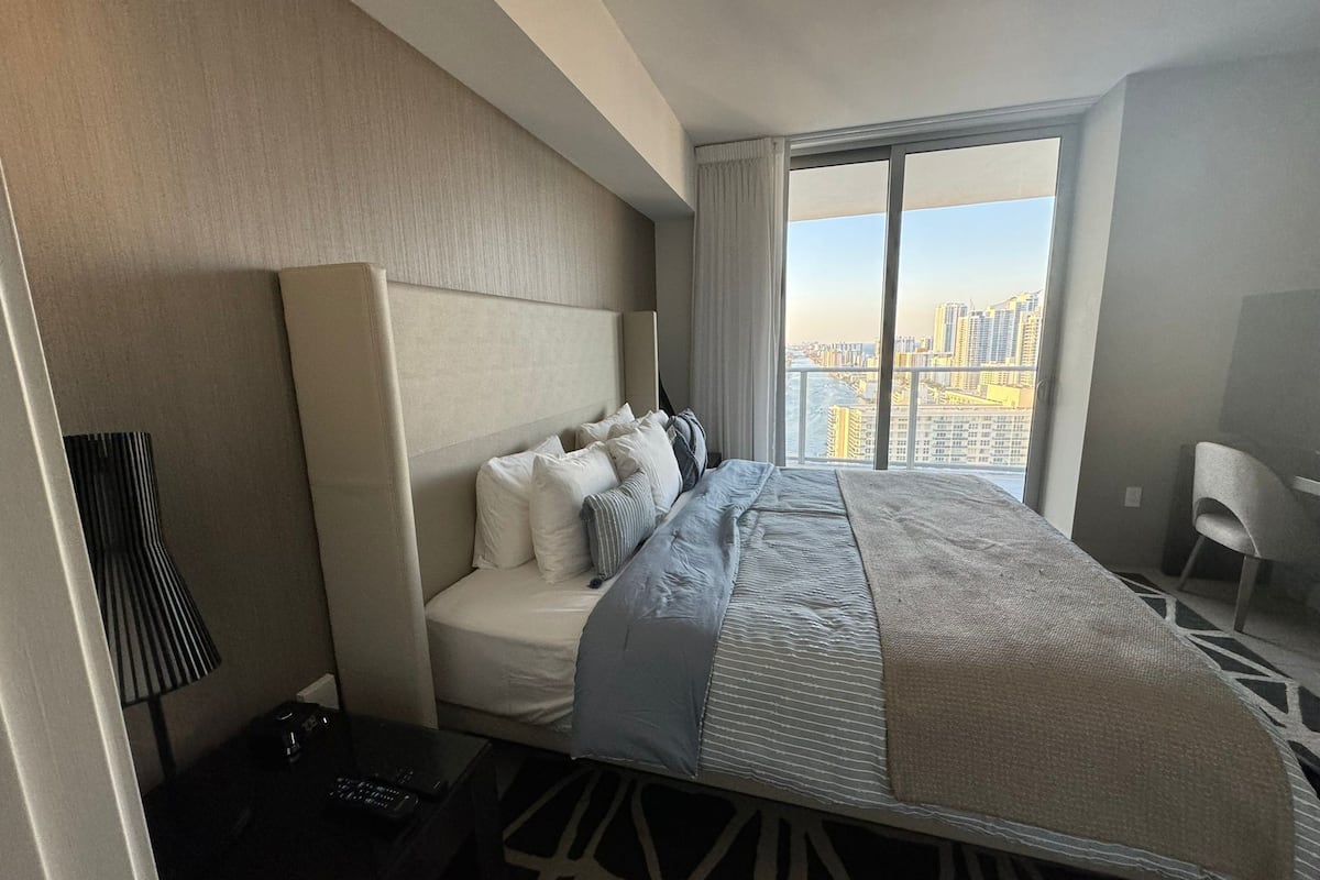 Quarto de hotel com uma cama grande, uma escrivaninha e vista para a paisagem urbana.