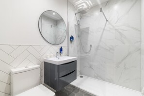 Um banheiro moderno com vaso sanitário branco, pia com armário preto, espelho redondo e chuveiro com box de vidro.