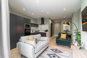 Uma sala de estar moderna com um sofá cinzento, uma poltrona verde e um tapete estampado.