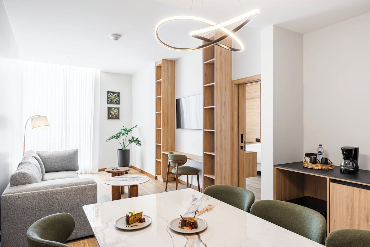 Uma sala de estar moderna com sofá, mesa de jantar e cadeiras. Há uma máquina de café e uma TV em um armário de madeira.
