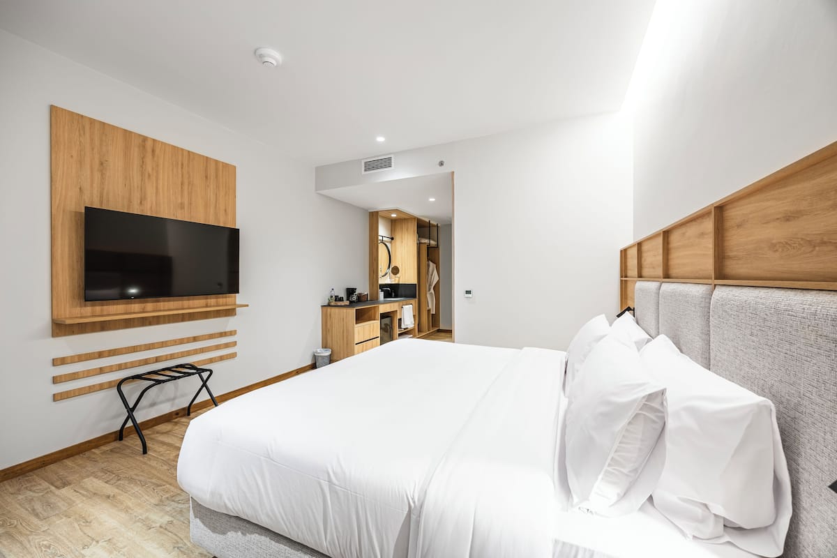 Quarto de hotel moderno com uma cama grande, uma televisão montada e uma cabeceira de madeira.