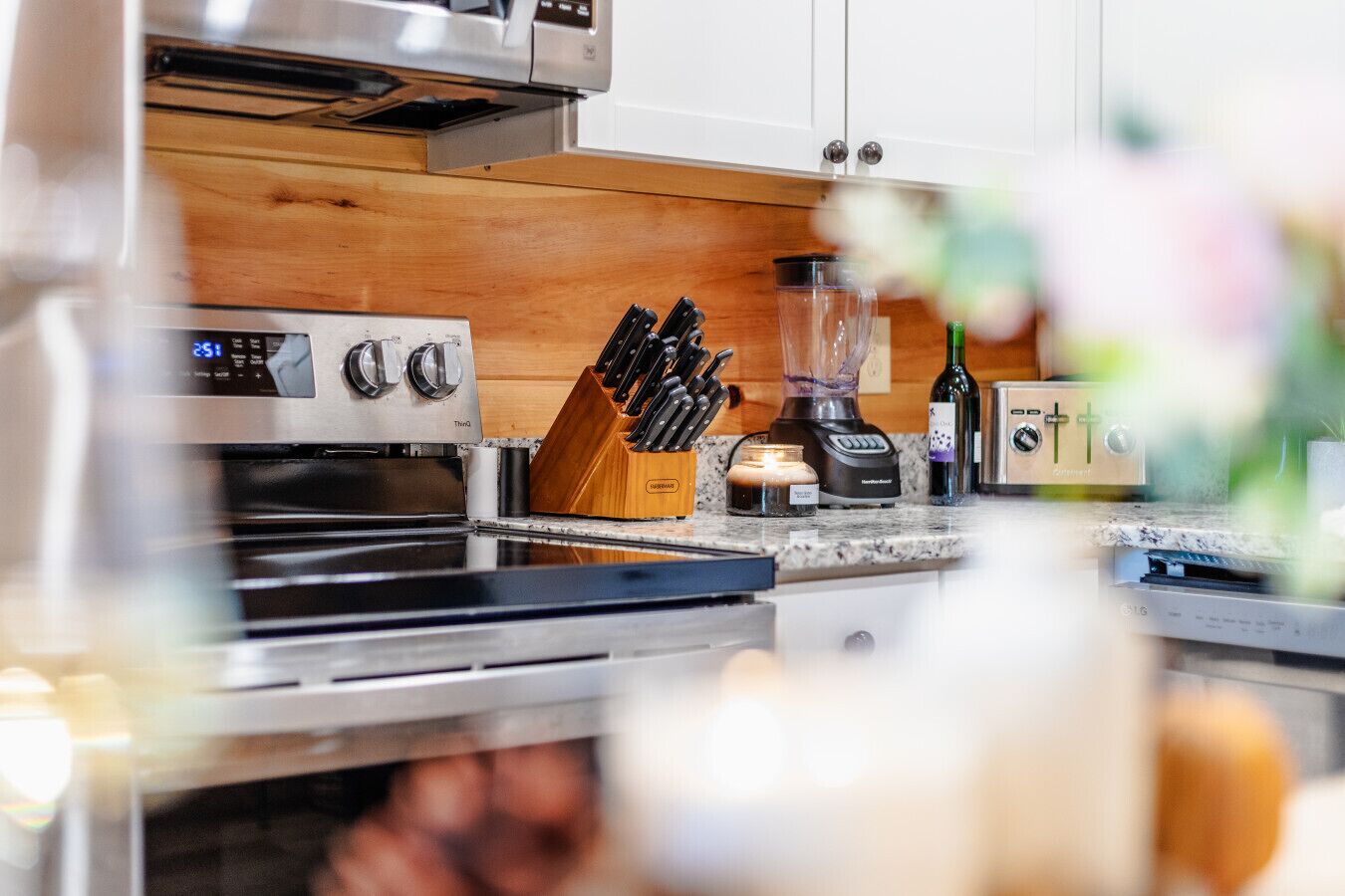Uma cozinha moderna com eletrodomésticos de aço inoxidável, escorredor de facas, liquidificador e uma garrafa de vinho.