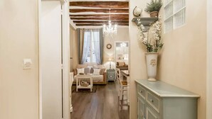 Uma sala de estar acolhedora com um sofá, uma mesa de centro e um candeeiro. Há um espaço de jantar com uma mesa e cadeiras. O quarto possui piso de madeira e um armário azul claro.