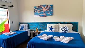 Quarto de hotel com duas camas, cada uma com roupa de cama azul e almofadas em formato de estrela-do-mar, um quadro de estrela-do-mar na parede e piso de madeira.