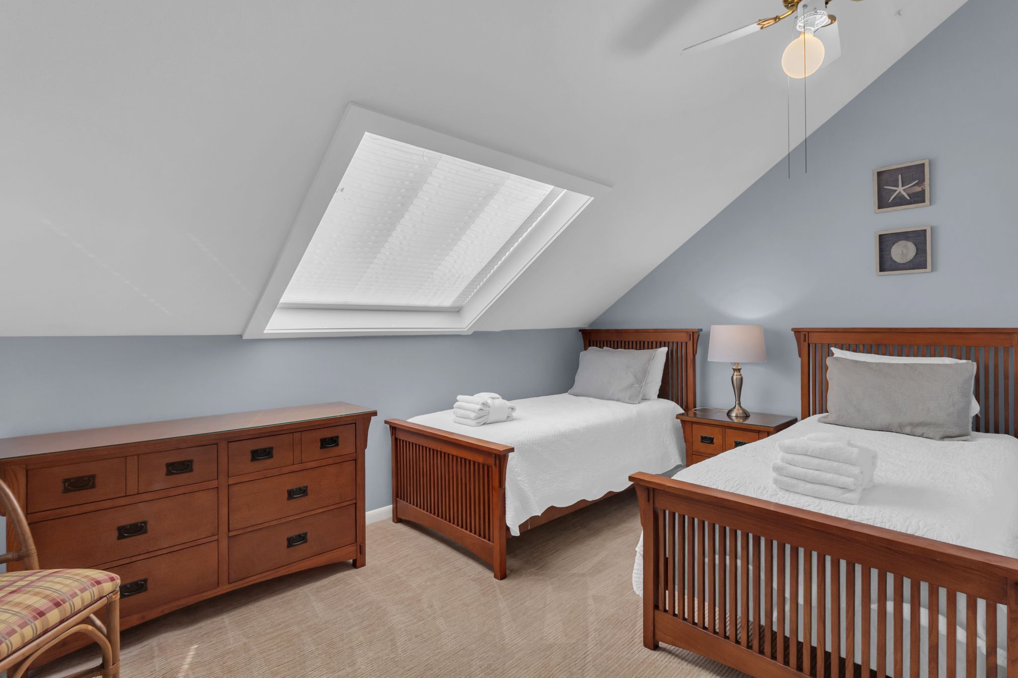 Quarto com duas camas, cómoda de madeira, cadeira, ventoinha de teto e clarabóia.