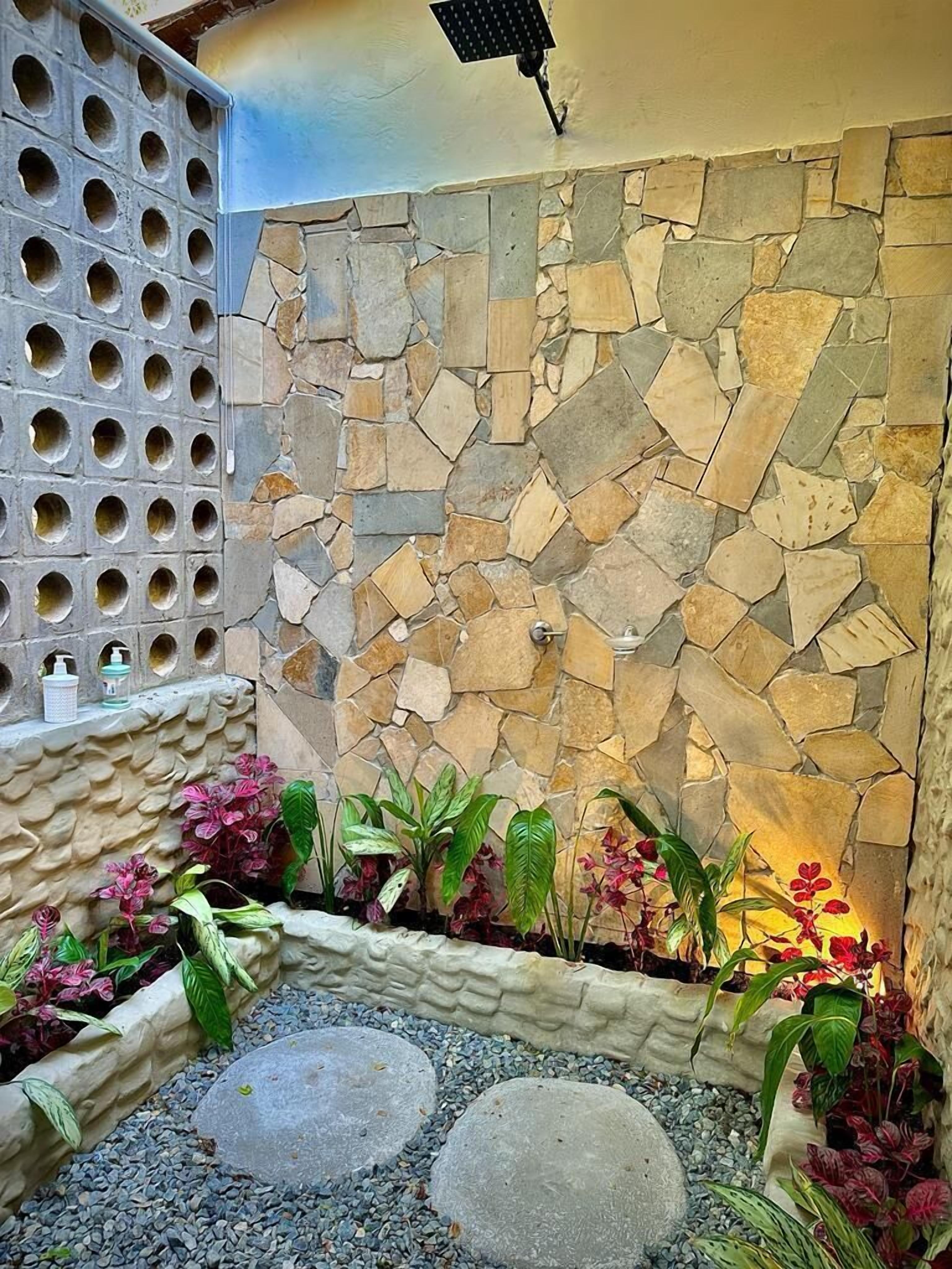 Mural de pedra com diversas plantas e uma cerca metálica decorativa.