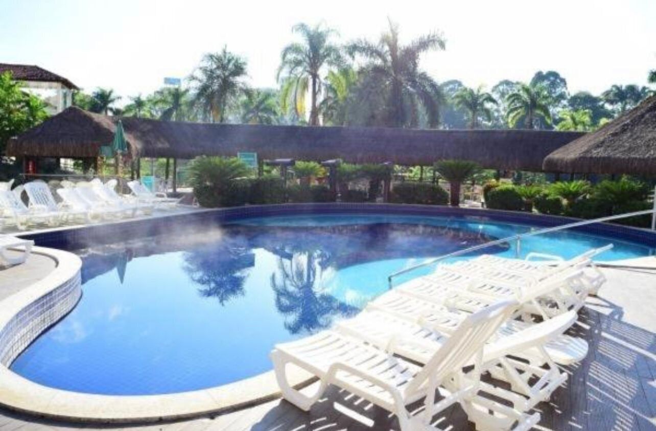 Piscina com espreguiçadeiras e estruturas com telhado de palha.