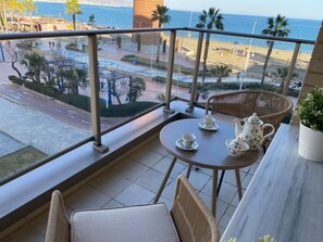 Uma varanda com móveis de vime, uma mesa e vista para a praia e o oceano.