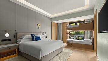 Quarto de hotel moderno com uma cama grande, uma escrivaninha, uma mesa de cabeceira, telefone fixado na parede, luminária na parede e uma janela com vista para o verde.