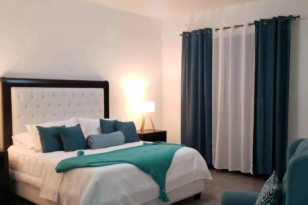 Quarto bem arrumado com cama, mesas de cabeceira, uma cadeira e cortinas.