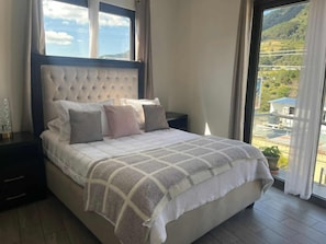 Quarto com uma cama grande, mesa de cabeceira e vista para o exterior.