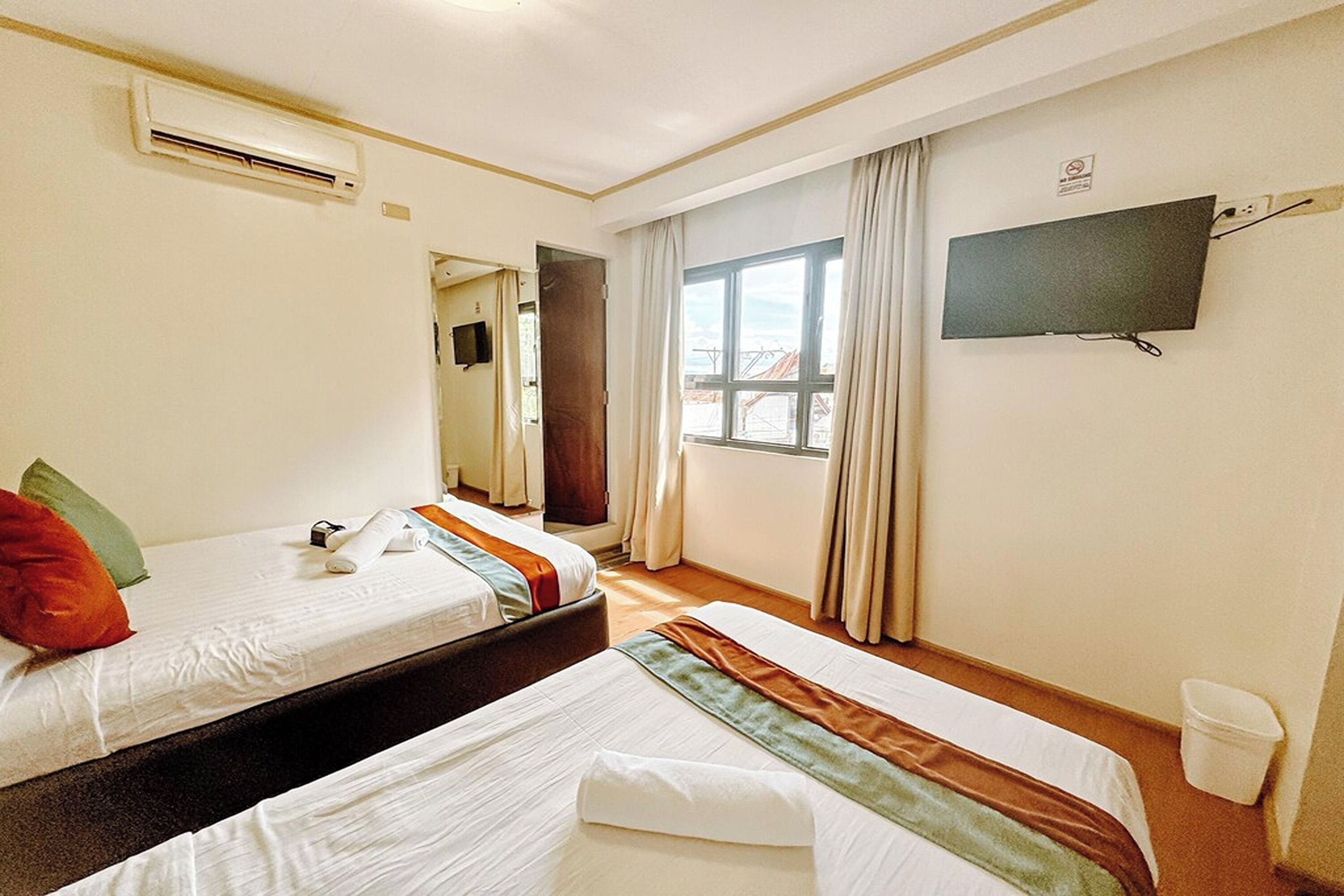 Quarto de hotel com duas camas, uma televisão presa na parede e uma janela com cortinas.