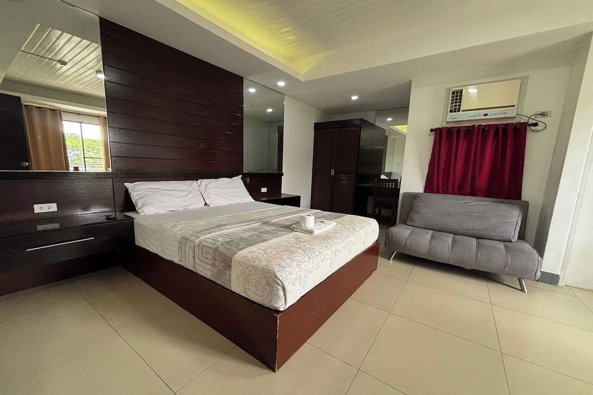 Quarto moderno com uma cama grande, um sofá cinzento, um guarda-roupa e um espelho.