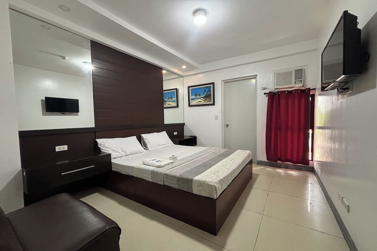 Quarto com cama grande, televisão na parede, espelho e cortina vermelha.