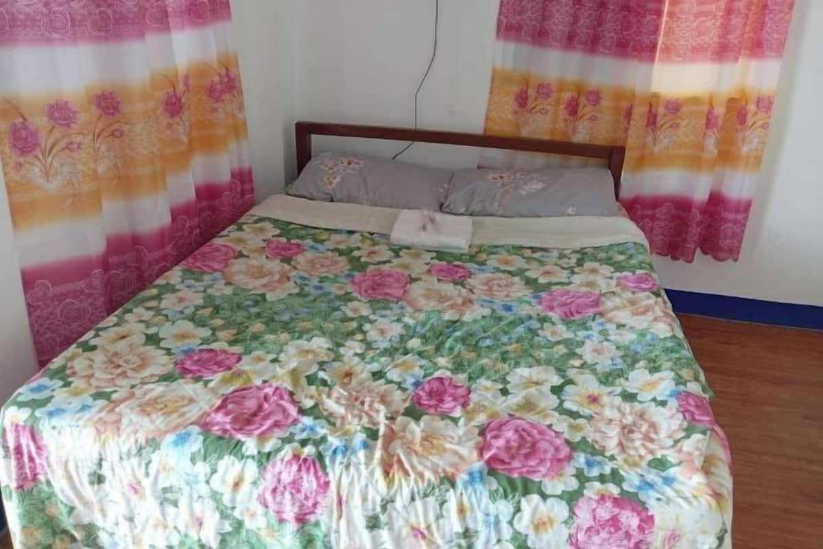 Uma cama com roupa de cama florida, cortinas estampadas com flores e cabeceira de madeira.